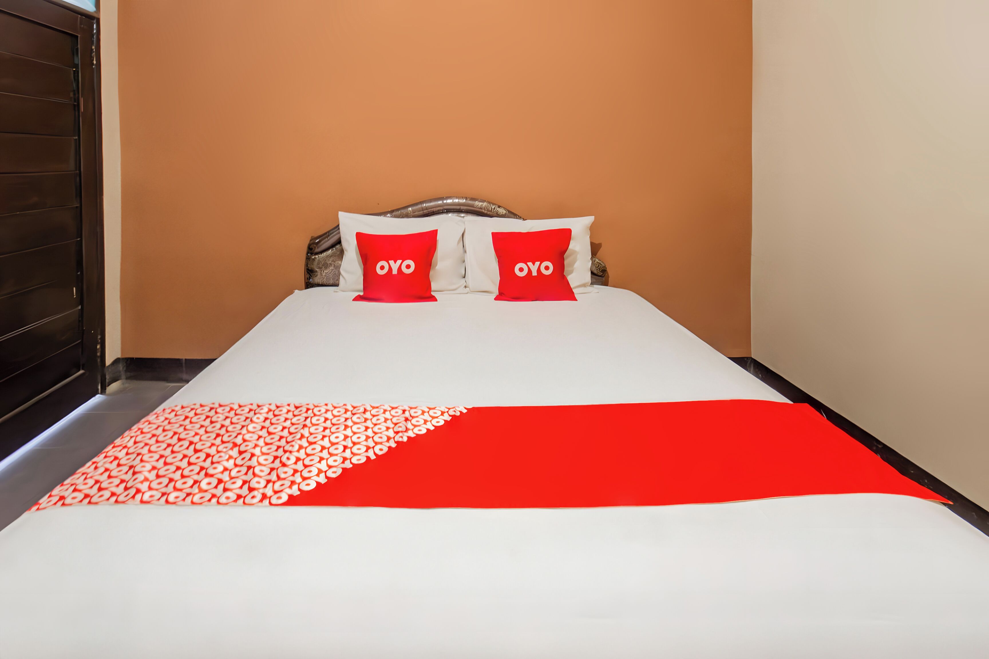 Quarto de hotel com uma cama, duas almofadas com o logotipo 'OYO' e um cobertor vermelho e branco.