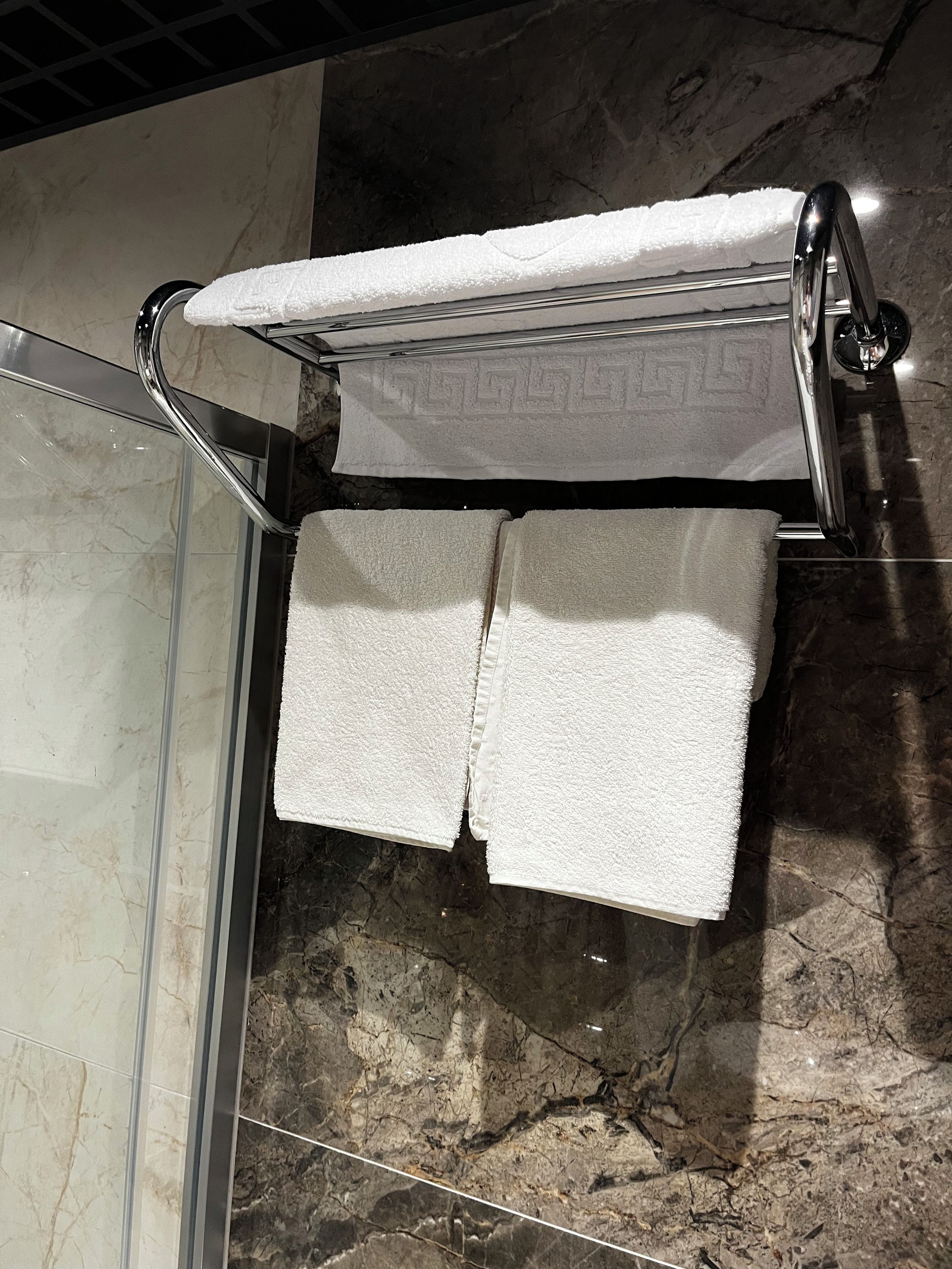 Casa de banho com cabine de chuveiro em vidro, toalheiro cromado e chão em mármore.