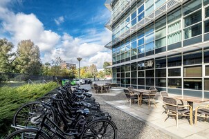 Um edifício moderno com fachada de vidro, área de estar ao ar livre e uma fileira de bicicletas estacionadas na frente.