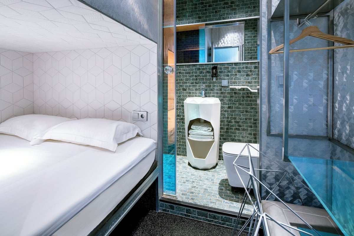 Quarto de hotel moderno com cama, box de vidro para o chuveiro e vaso sanitário.