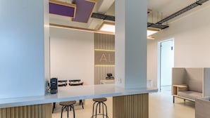 Uma área de recepção moderna, com balcão, banquetas e um espaço de estar com sofá e uma mesa pequena.