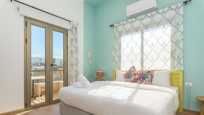 Quarto com cama, janela com cortinas estampadas, mesa de cabeceira com abajur e vista para o exterior.
