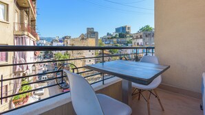 Varanda com mesa e cadeiras, vista para um horizonte urbano com diversos edifícios e céu claro.