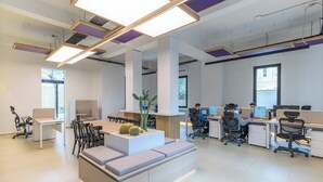 Um espaço de escritório moderno com cubículos, uma área de estar central e janelas amplas.