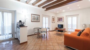 Uma sala de estar moderna com um sofá, uma mesa de jantar com cadeiras, uma televisão e obras de arte nas paredes.