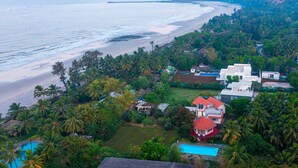 Um imóvel à beira-mar com vista para a praia, vegetação exuberante e piscina.