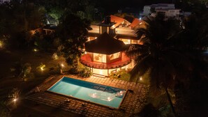 Uma casa bem iluminada, com dois andares e uma piscina em primeiro plano.