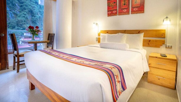 Quarto de hotel com uma cama grande, cabeceira de madeira, mesas de cabeceira e vista para uma varanda florida.