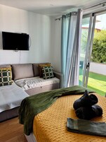 Quarto de hotel moderno com uma cama, um sofá, televisão de tela plana e porta de vidro deslizante para uma varanda.