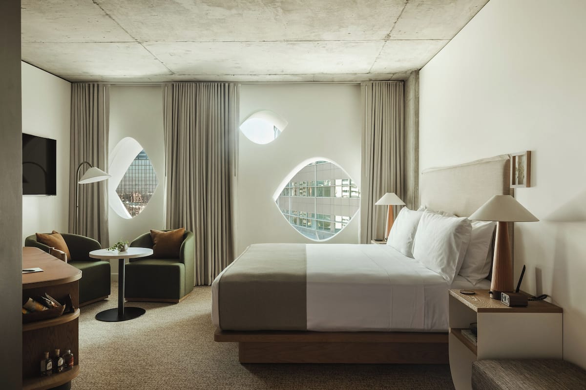 Quarto de hotel moderno com uma cama grande, duas áreas de estar, uma janela redonda e uma TV.