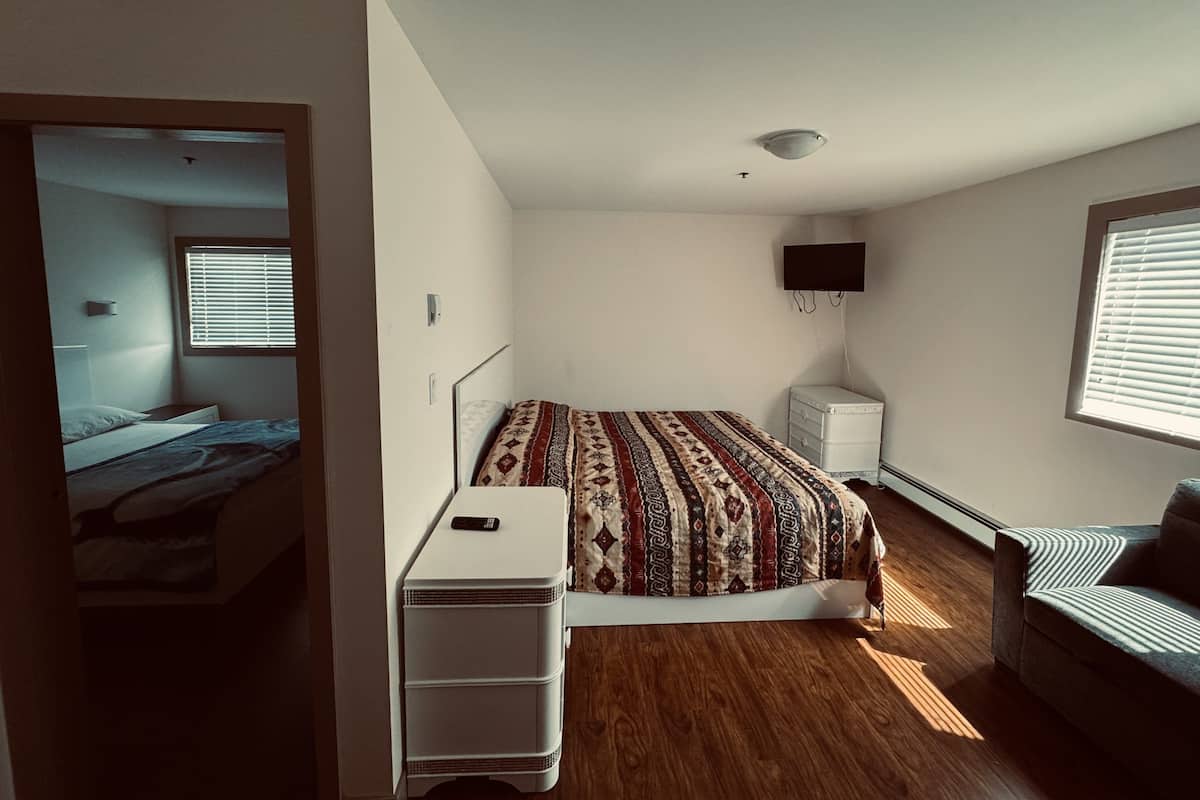 Quarto com cama, mesa de cabeceira, penteadeira, televisão e janela com persianas.