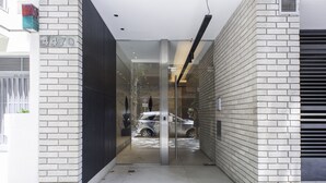 Entrada de um edifício moderno com porta de vidro, um carro visível do lado de fora e um muro de tijolos.