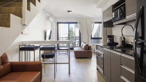 Um apartamento moderno com cozinha, sala de jantar e sala de estar. Possui uma escada, um sofá, uma mesa de jantar com cadeiras e uma janela grande com cortinas.