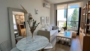 Uma sala de estar moderna com uma mesa de mármore, sofá branco e uma varanda com vista para a cidade.