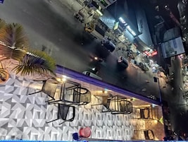 Vista da rua à noite, com um restaurante que apresenta padrões geométricos nas paredes e mesas externas com cadeiras de metal.
