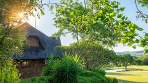Um edifício com telhado de colmo, cercado por vegetação exuberante e um campo de golfe ao fundo.