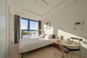 Quarto de hotel moderno com uma cama grande, uma mesinha redonda e vista para a cidade através de uma janela ampla.