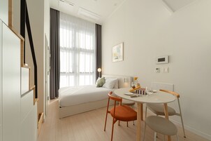 Quarto de hotel moderno com cama, mesa de jantar com cadeiras, janela com cortinas e termostato fixado na parede.