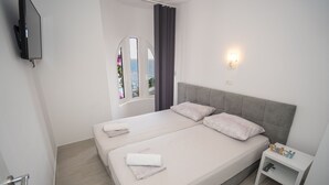 Quarto de hotel moderno com uma cama grande, mesa de cabeceira, TV fixada na parede e janela com vista.