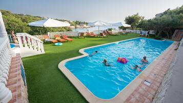 Piscina com borda azulejada, rodeada por gramado e espreguiçadeiras.