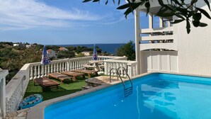 Área da piscina com vista para o mar, cadeiras de descanso e guarda-sóis.