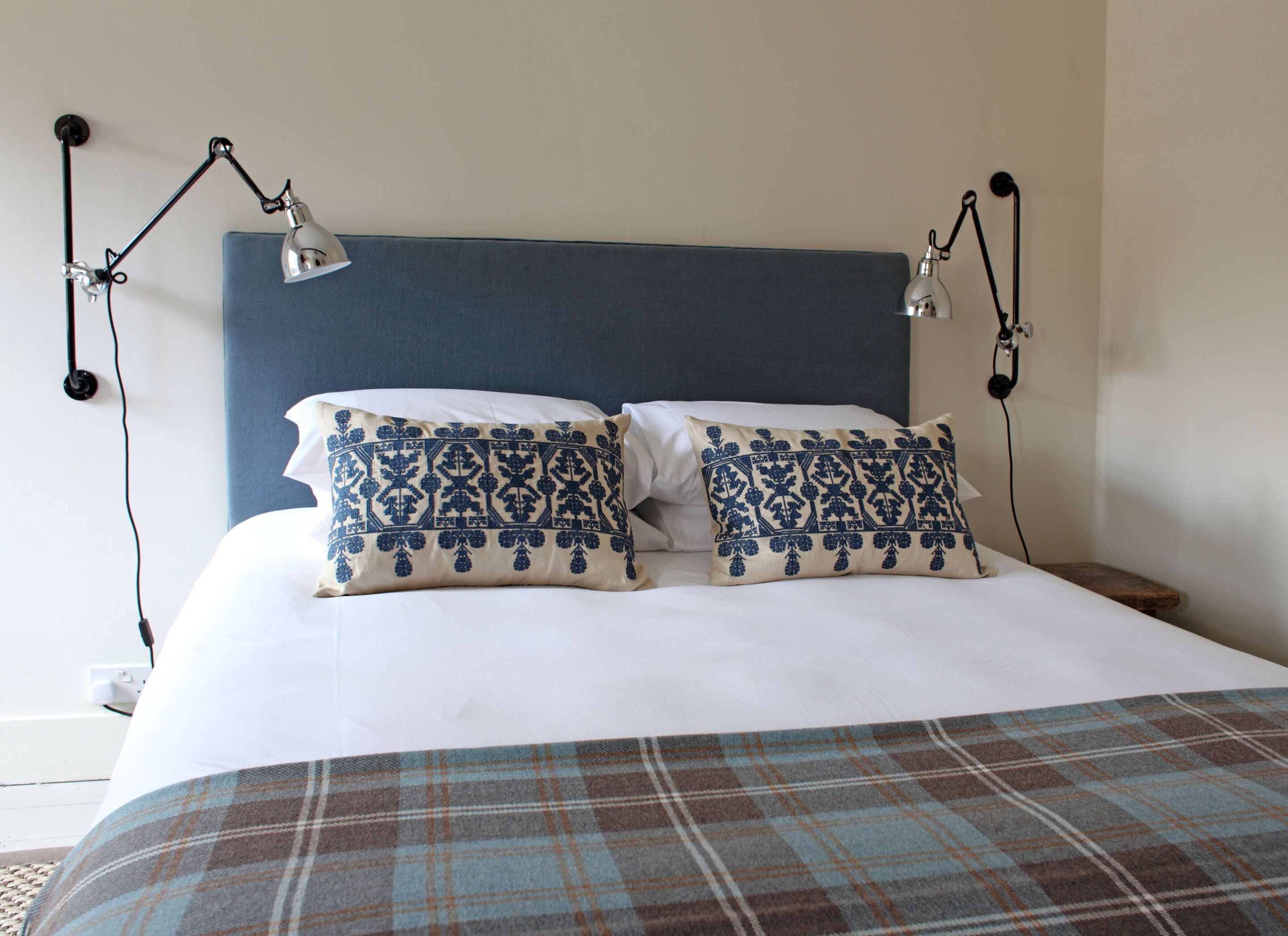 Uma cama com cabeceira azul, duas almofadas decorativas e um cobertor xadrez.