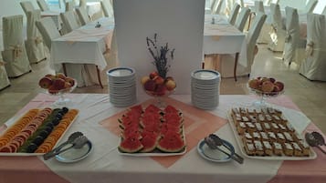 Mesa de buffet com diversas travessas de fruta, incluindo melancia e pêssegos, e uma seleção de sobremesas.