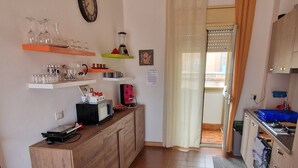 Uma cozinha compacta com bancada de madeira, máquina de café e lixeira.