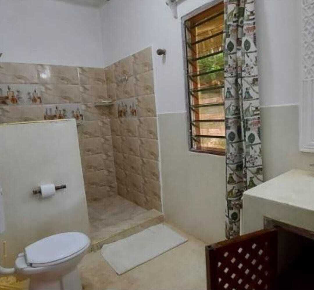Casa de banho com sanita, chuveiro e janela com cortinas estampadas.