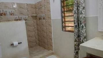 Casa de banho com sanita, chuveiro e janela com cortinas estampadas.