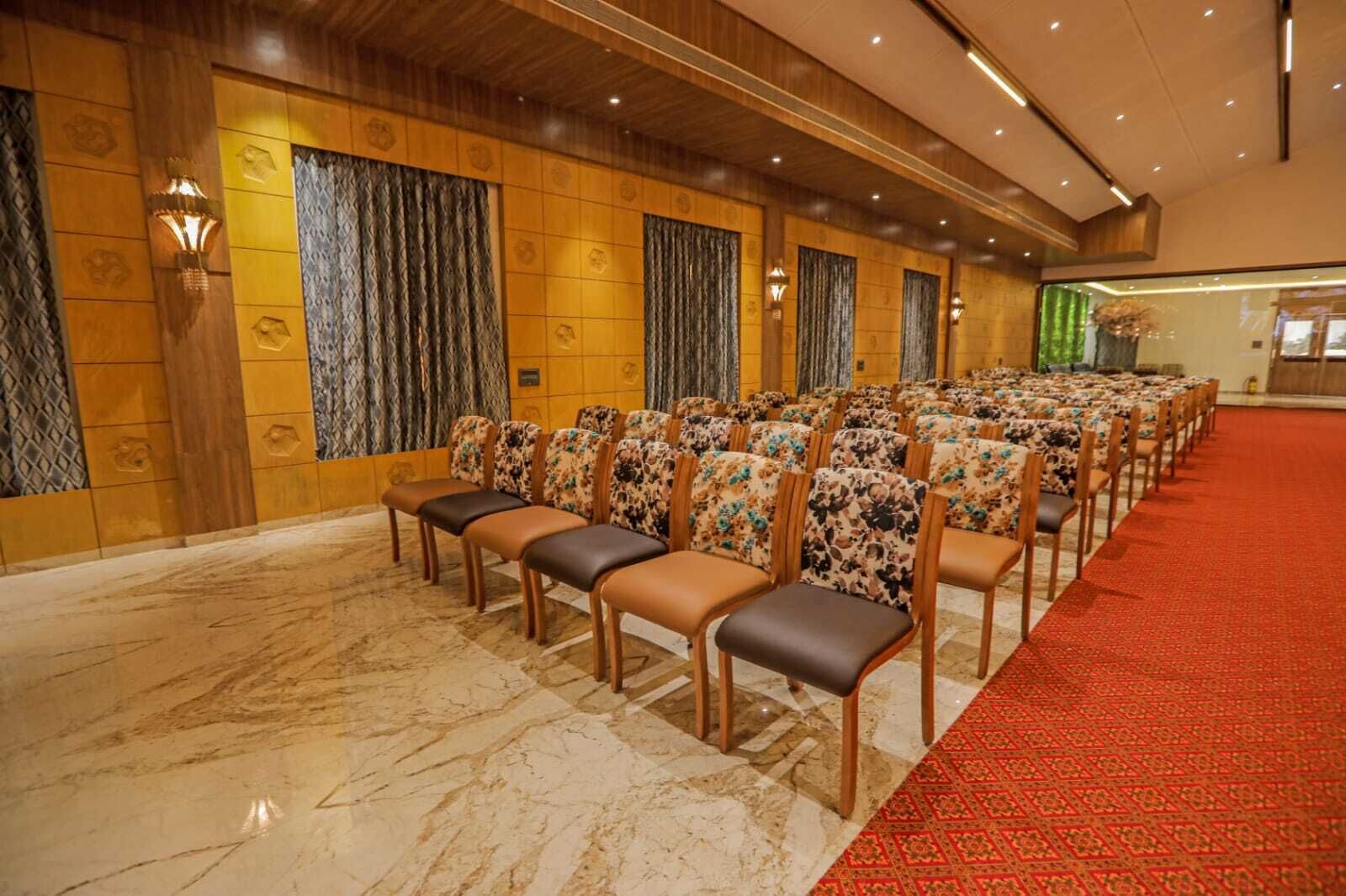 Uma sala de conferências com fileiras de cadeiras, um tapete vermelho e painéis de madeira nas paredes.