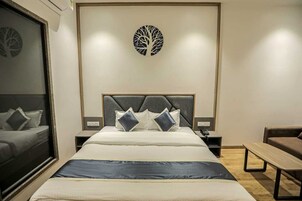 Quarto de hotel moderno com uma cama grande, cabeceira com design de árvore, mesa de cabeceira com telefone e um banco de madeira.
