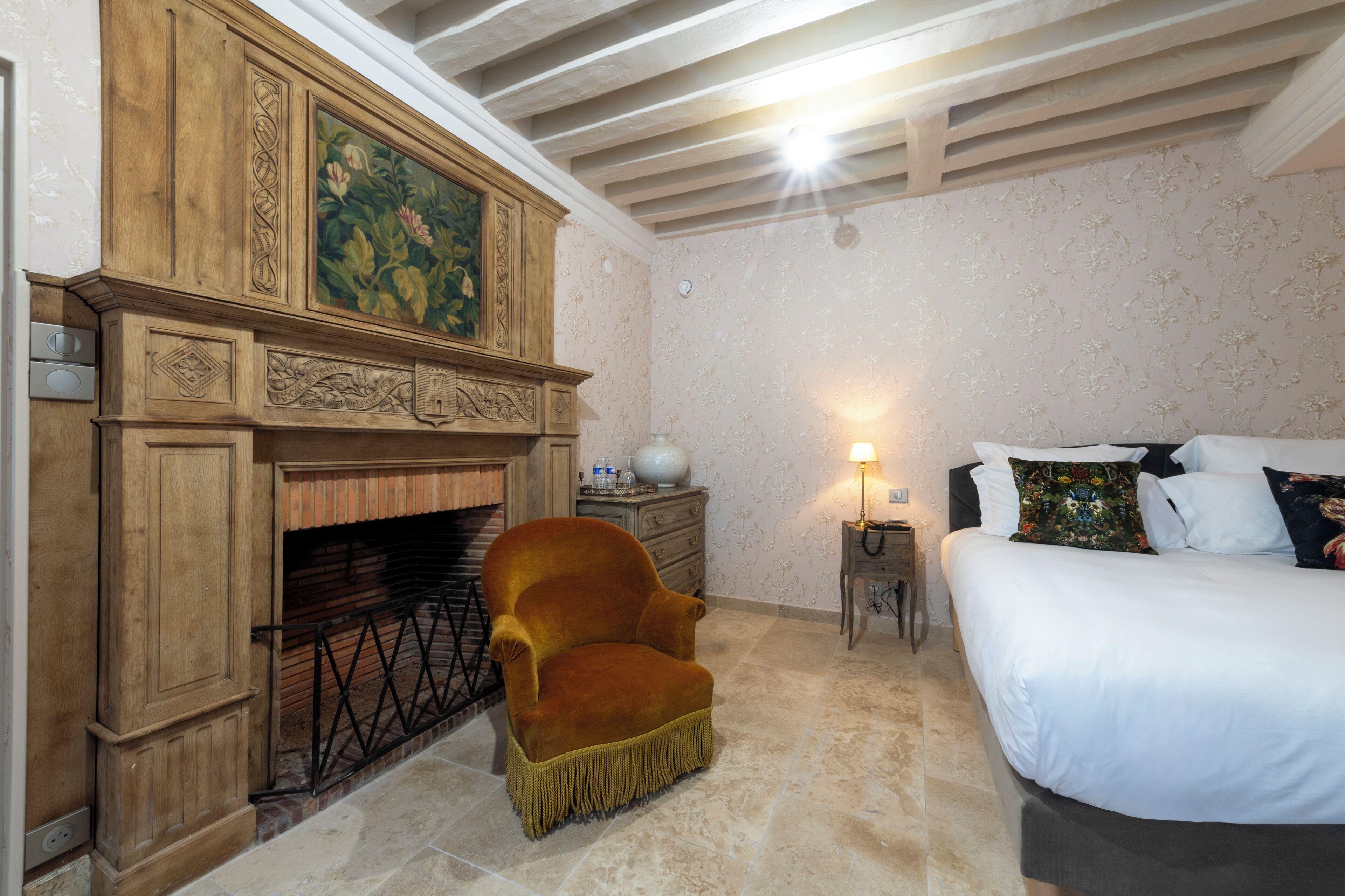 Um quarto com cama, poltrona, lareira e mesa de cabeceira.
