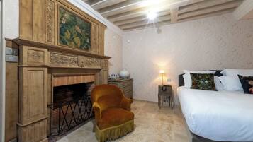 Um quarto com cama, poltrona, lareira e mesa de cabeceira.
