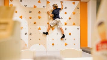 Uma criança escalando uma parede de madeira com pontos de apoio laranja e cinza.