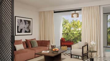 Uma sala de estar moderna com sofá, poltrona, mesa de centro e vista para palmeiras através de grandes janelas.