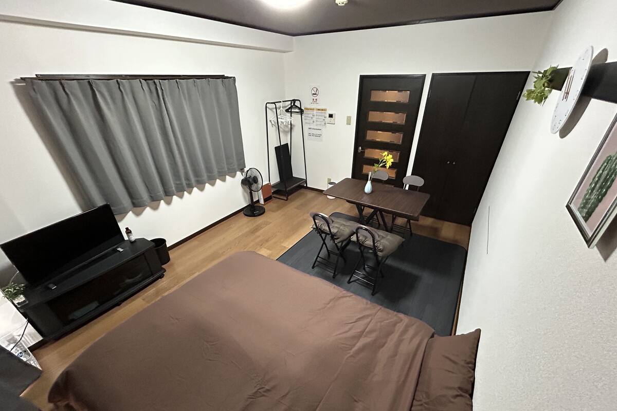 Quarto pequeno com cama, televisão, escrivaninha e cadeira.