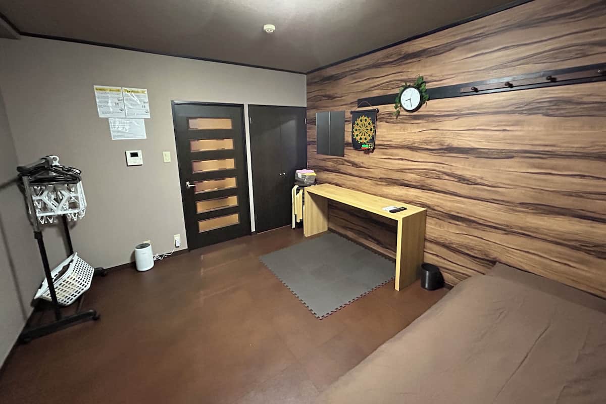 Quarto com parede de madeira, uma escrivaninha, um sofá, uma porta e um alvo de dardos.