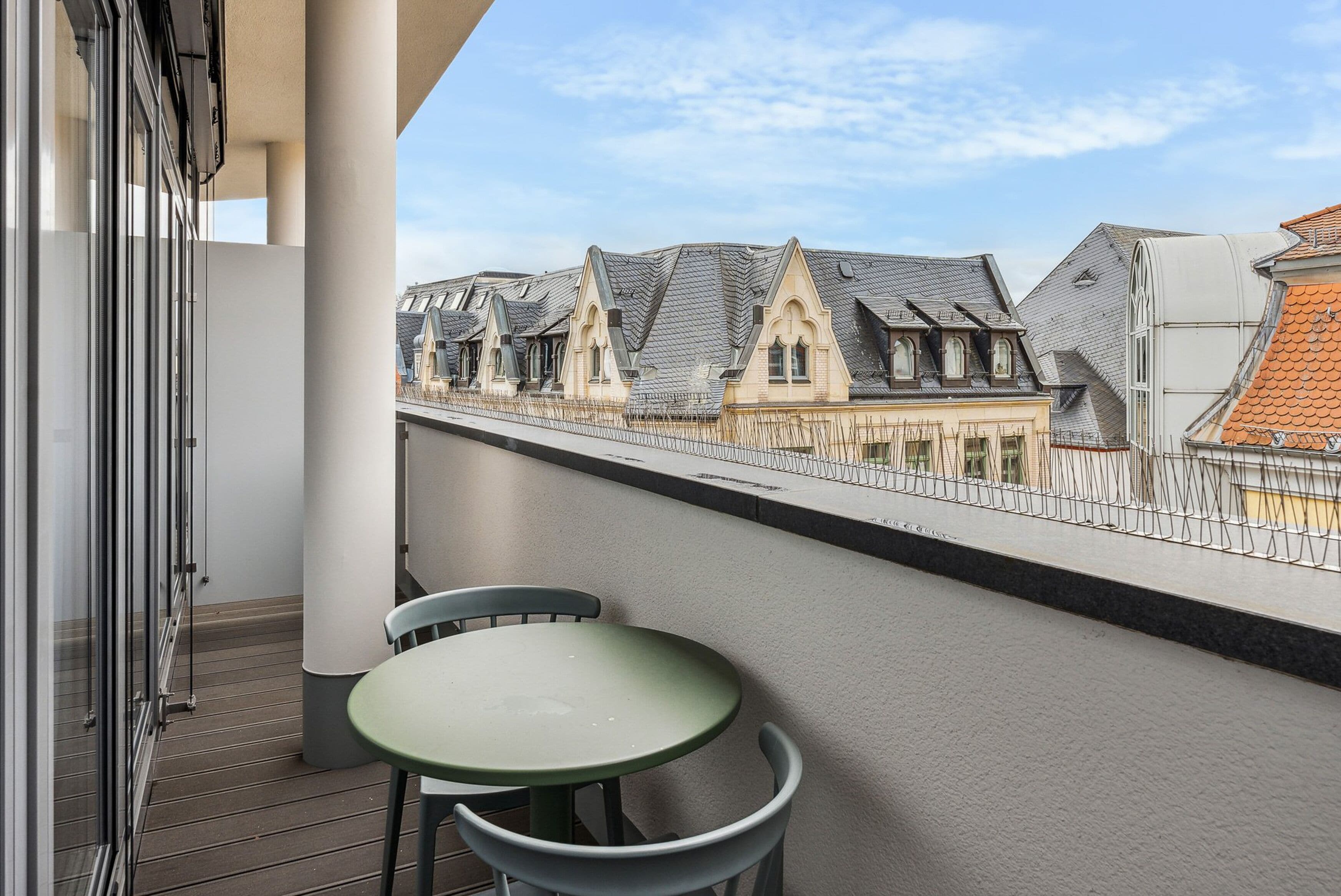 Uma varanda com mesa e cadeiras, com vista para uma fileira de casas tradicionais com telhados inclinados.