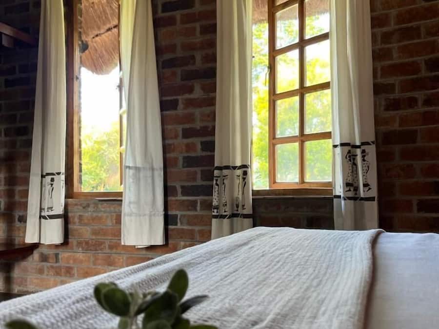 Quarto com parede de tijolos, janela com cortinas e cama com colcha branca.