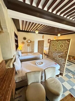 Quarto de hotel com duas camas, uma escrivaninha de madeira, um painel decorativo na parede e chão xadrez.