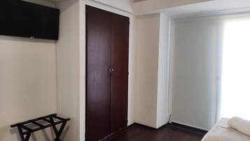 Quarto com armário de madeira escura, uma pequena mesa e uma cama com almofada branca.