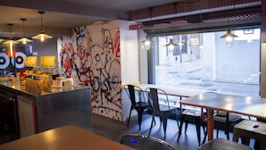 Interior de café moderno com arte de graffiti na parede, um balcão com produtos alimentícios e vista para a rua através de grandes janelas.