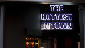 A entrada de um hostel com um letreiro de neon que diz "THE HOTTEST IN TOWN".