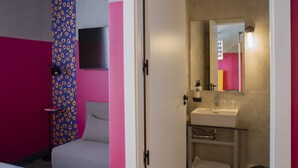 Quarto de hotel com cama, banheiro com pia e espelho, e porta que dá para outro cômodo.