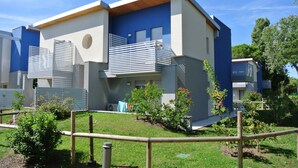 Um edifício moderno com fachada azul e branca, uma varanda e uma área de jardim cercada.
