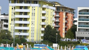 Um edifício com várias andares, varandas, área de piscina com guarda-sóis e céu claro.