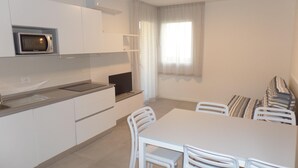 Uma cozinha moderna com armários brancos, micro-ondas embutido e área de jantar com mesa e cadeiras brancas.