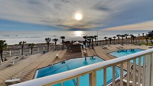 Área de piscina com duas piscinas, uma praia e vista para o pôr do sol.