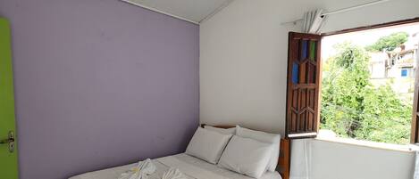 Quarto com cama, ventoinha no teto, janela com vista e porta verde.